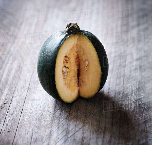 A green squash, sliced to show the centre, on a wooden surface - Royalty-free Stock Photo | Dissolve
