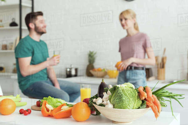 Vegan couple talking in kitchen with fruits and vegetables on ...