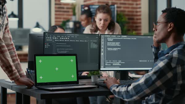 Programer taking glasses off talking with colleague at desk with laptop with green screen chroma ...