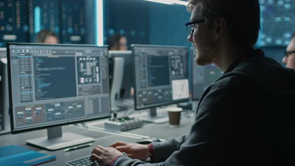 Smart male it programer working on desktop computer in data center technical system control room ...