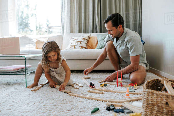 Girl assembling toy train while sitting with father in living room at home - Royalty-free Stock ...