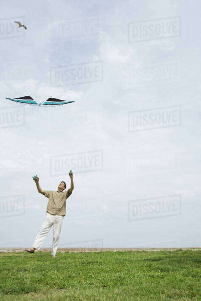 Man flying kite, arms raised, full length - Stock Photo - Dissolve