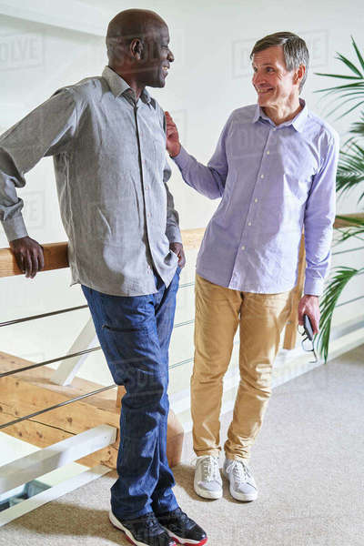 Two diverse middle-aged male friends chatting at home - Royalty-free Stock Photo | Dissolve