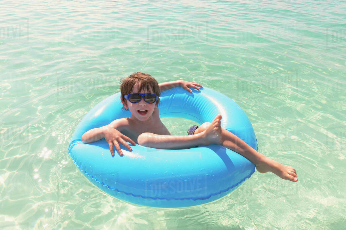 Portrait smiling boy in sunglasses floating in blue inflatable ring in ...