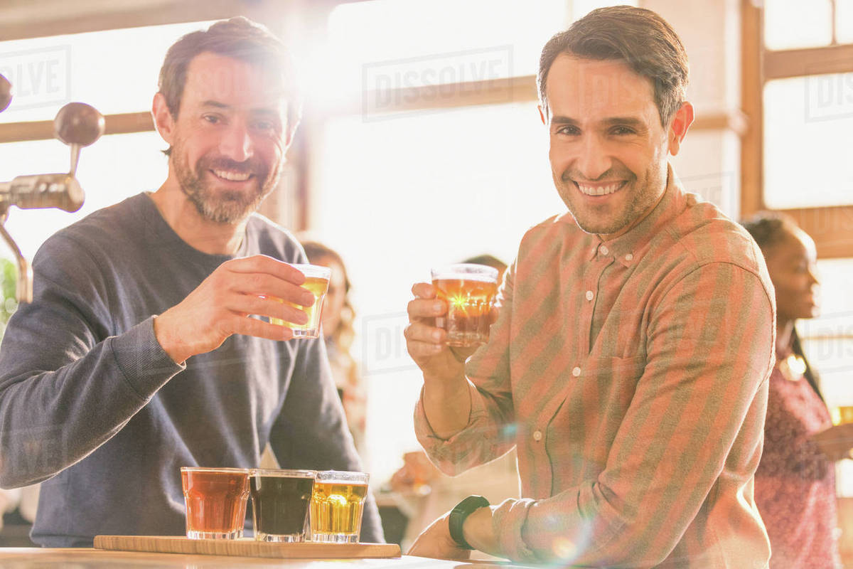 Portrait smiling men friends sampling beer at microbrewery bar ...