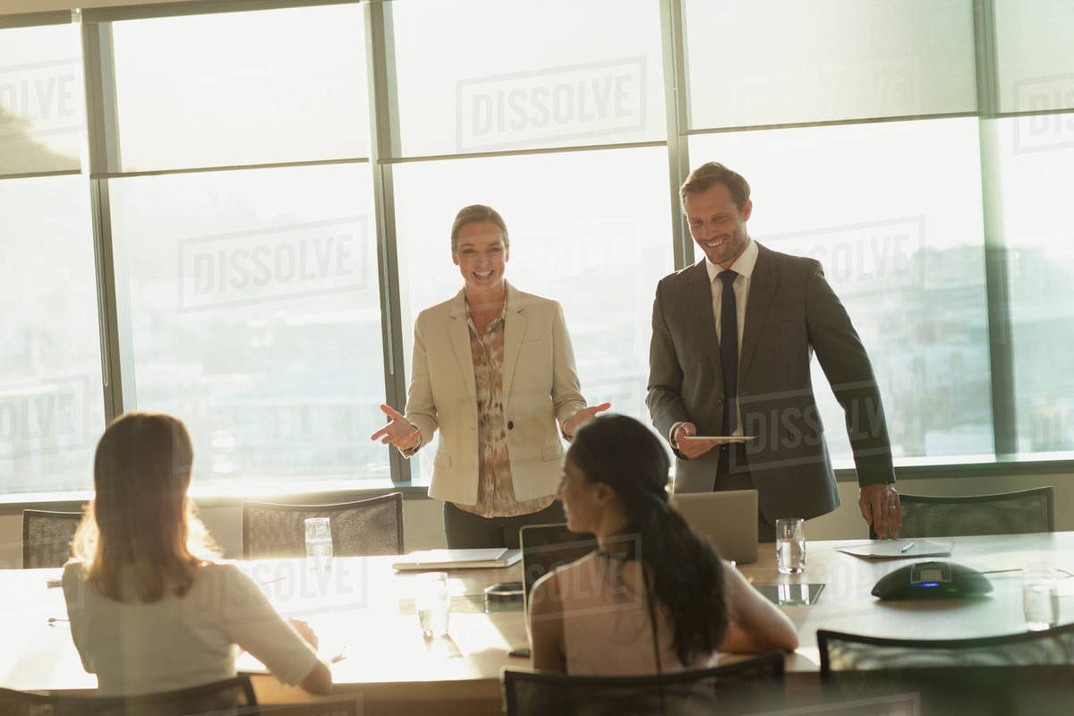 Smiling business people talking in sunny conference room meeting ...