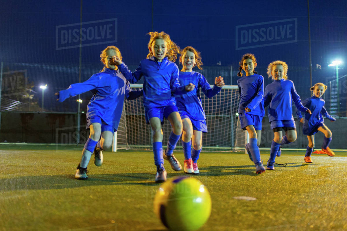 Girls soccer team playing, running toward ball on field at night ...