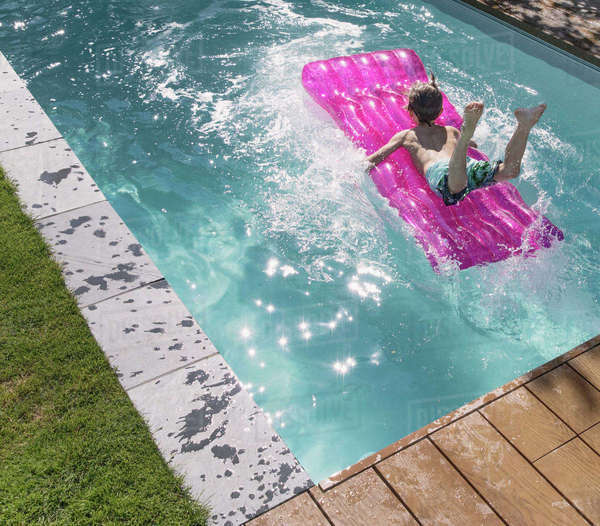 Playful boy jumping on inflatable raft in sunny summer swimming pool ...