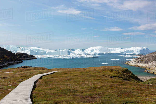 Sunny footpath leading to beach overlooking icebergs Greenland ...