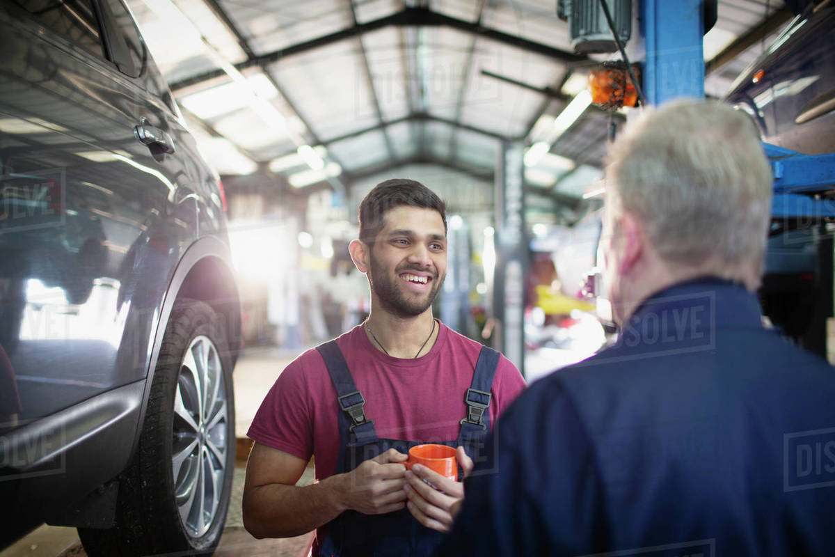 Smiling, happy male mechanics talking and drinking coffee in auto ...