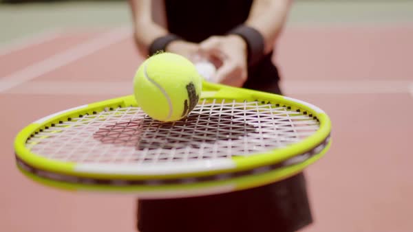 Female tennis player balancing a neon yellow tennis ball on her racket ...