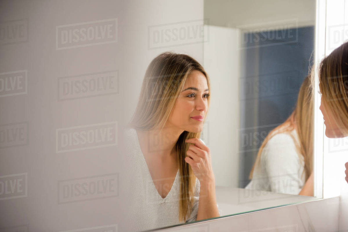 Young woman looking in mirror - Stock Photo - Dissolve