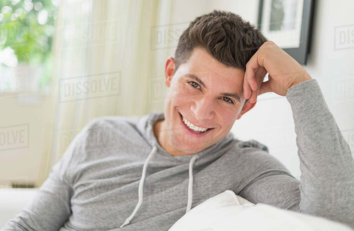 Young man sitting on sofa and smiling - Stock Photo - Dissolve