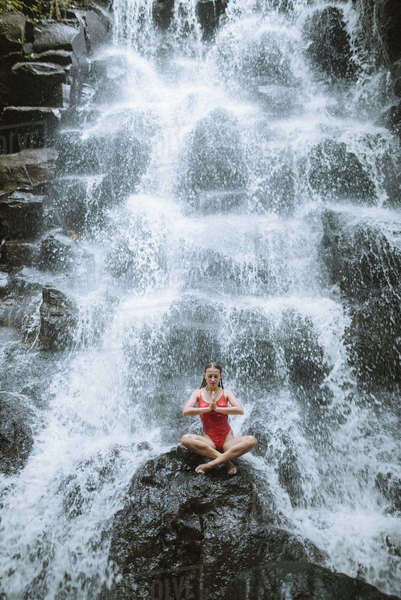 Woman wearing red swimsuit sitting by waterfall in Bali, Indonesia ...