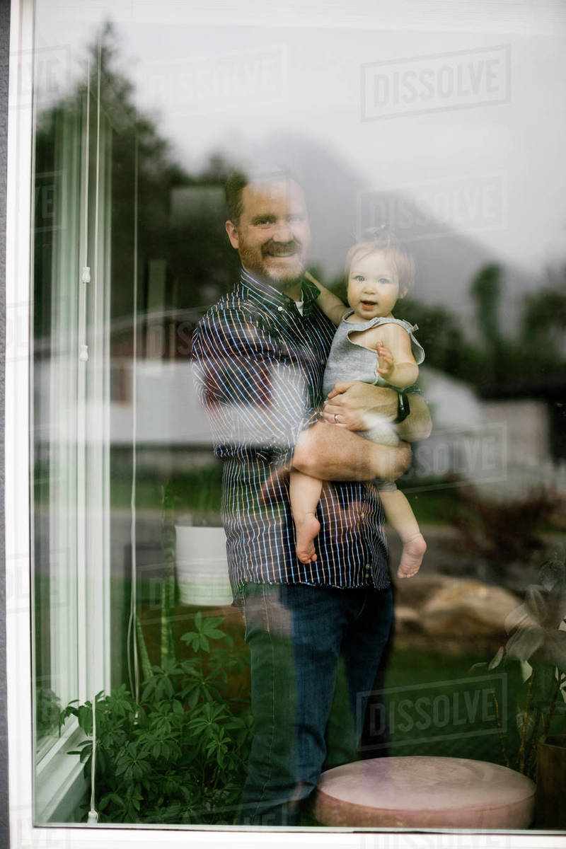 Father holding his daughter behind window - Stock Photo - Dissolve