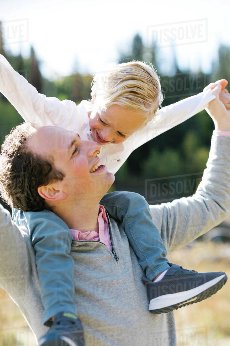Son sitting on father's shoulders in nature - Stock Photo - Dissolve
