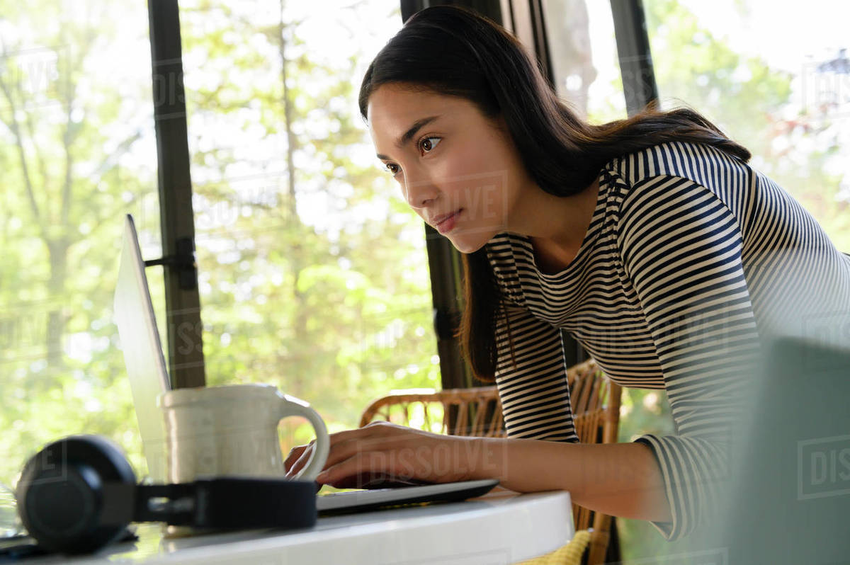 Woman leaning over table using laptop - Royalty-free Stock Photo | Dissolve