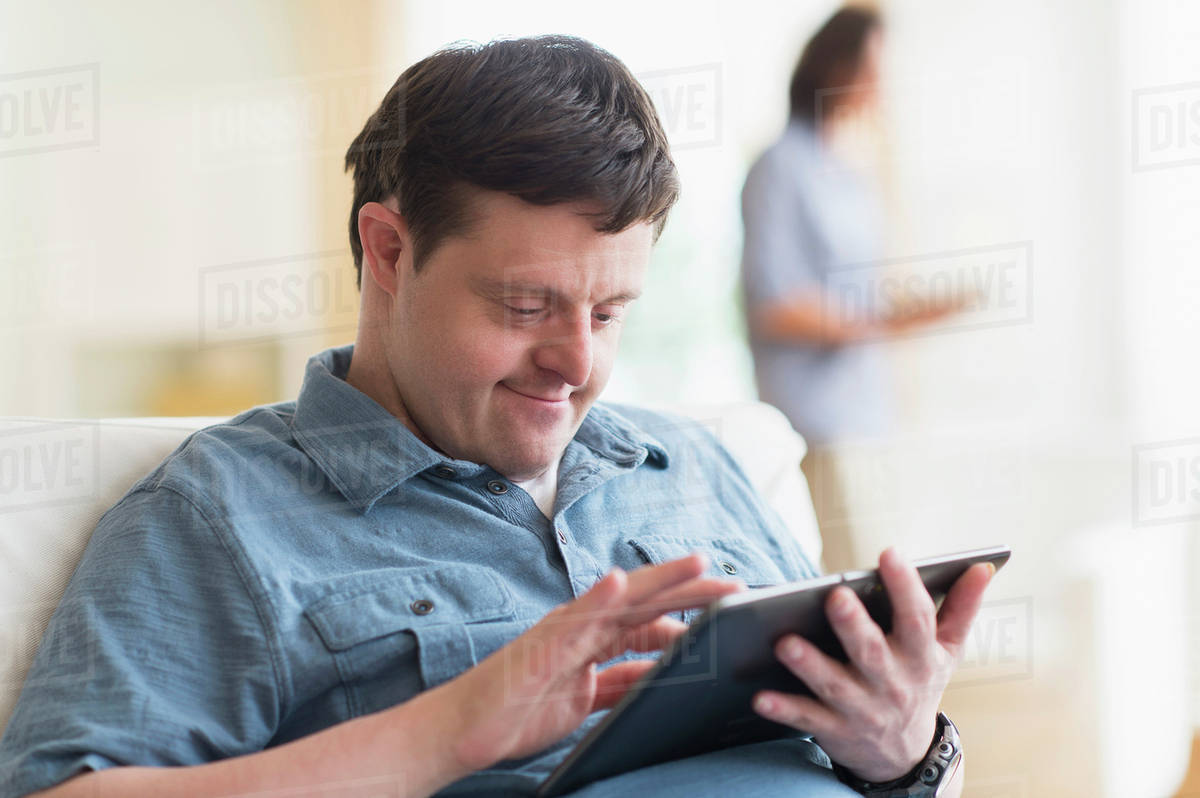Man with down syndrome using tablet - Stock Photo - Dissolve