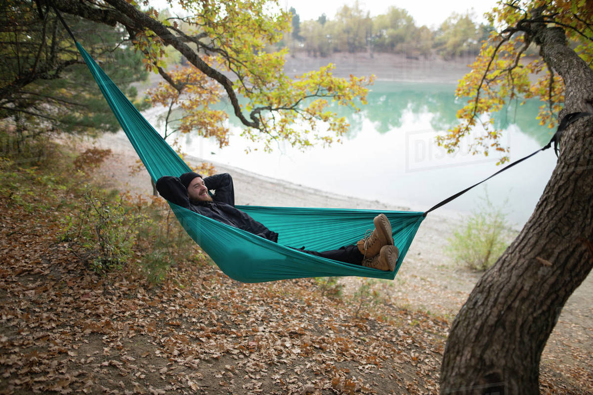 Italy, Smiling man lying in hammock near lake - Royalty-free Stock ...