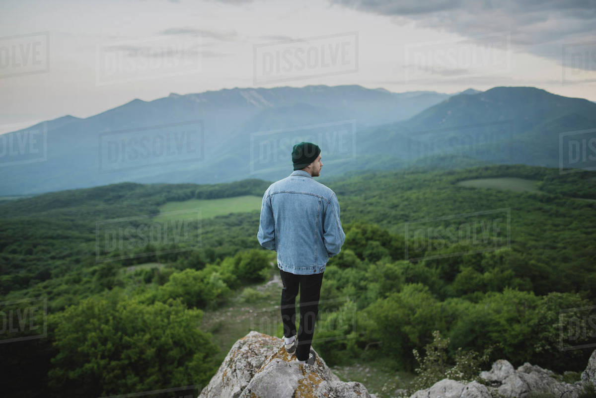 Man standing on cliff by mountain and forest - Stock Photo - Dissolve