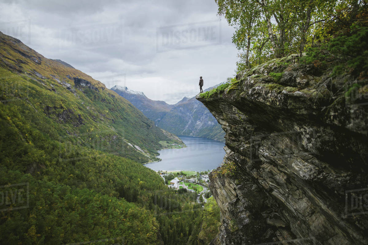 Norway, Geiranger, Man standing on edge of steep cliff above ...