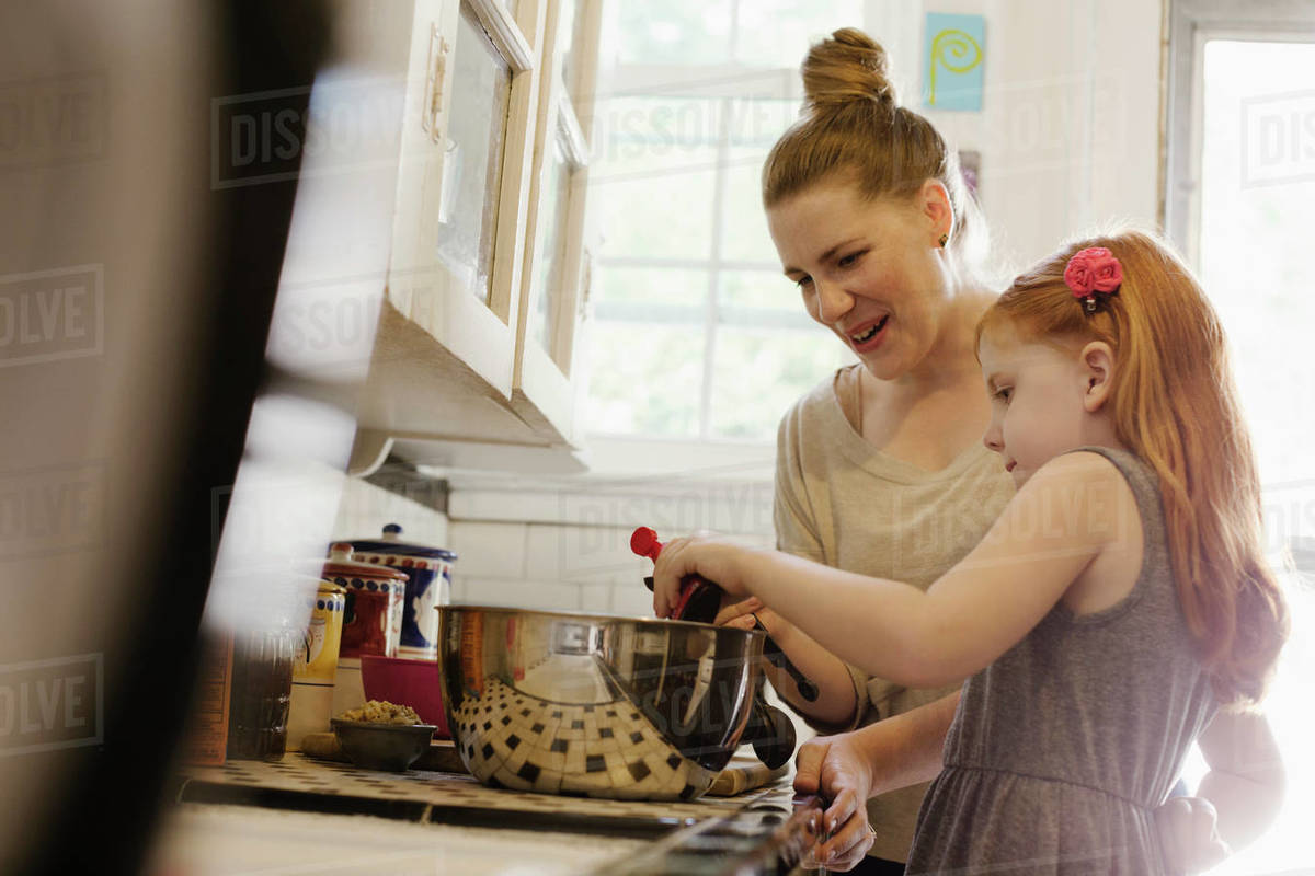 Mid adult mother giving daughter a helping hand in kitchen - Stock ...