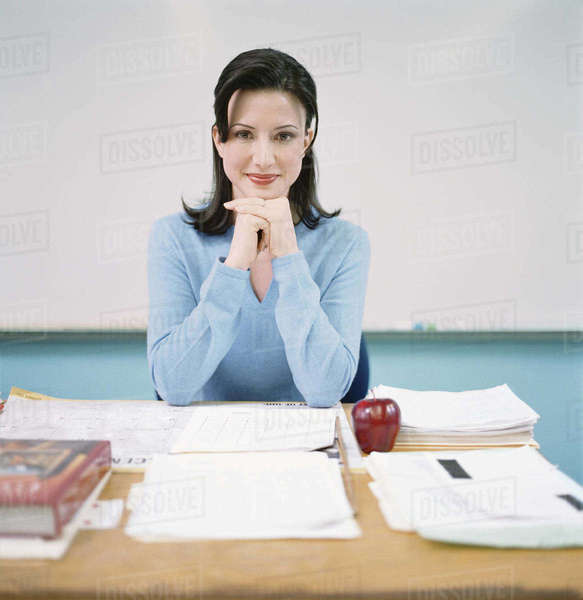 Portrait of teacher sitting behind desk - Stock Photo - Dissolve