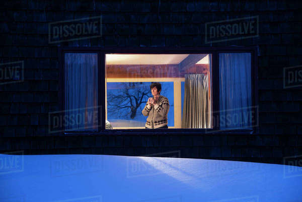Woman looking through window at dusk in winter - Stock Photo - Dissolve