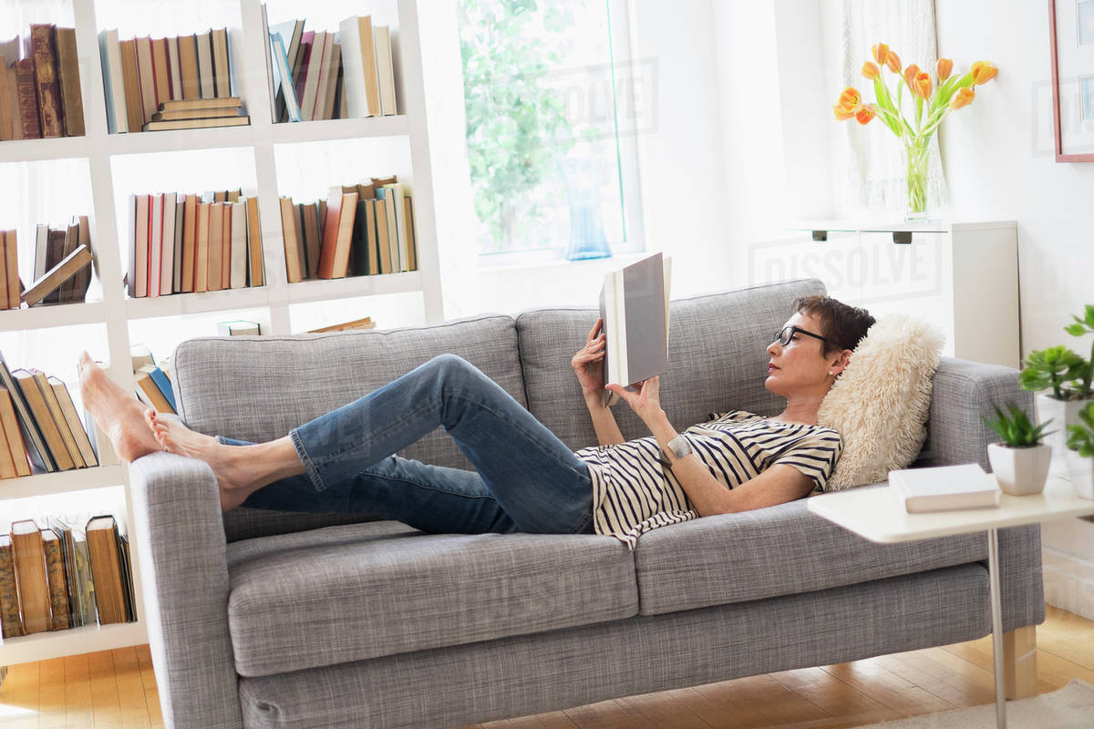 Senior woman reading book on sofa - Royalty-free Stock Photo | Dissolve