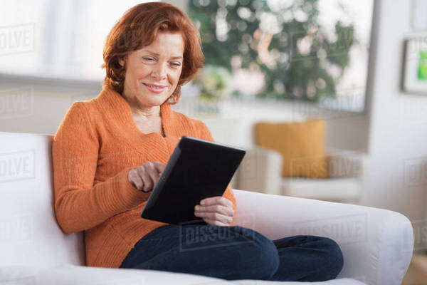 Woman sitting on sofa using digital tablet - Stock Photo - Dissolve