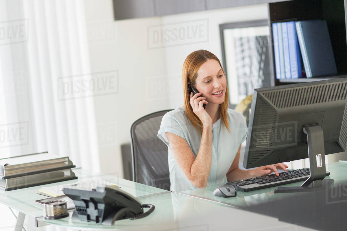 Business woman using computer and phone in office - Stock Photo - Dissolve