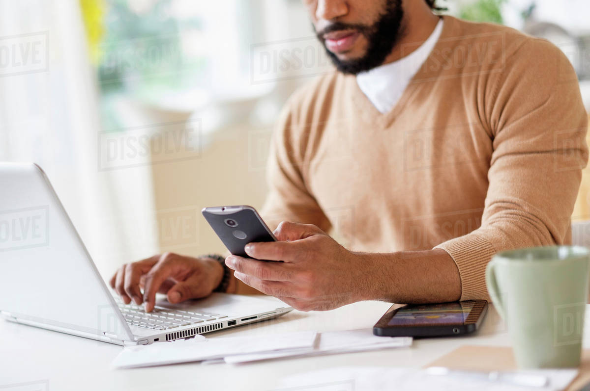 Man working with laptop at table and holding smart phone - Royalty-free ...