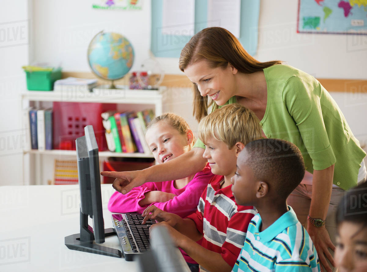 School children (8-9) with female teacher working with computers ...