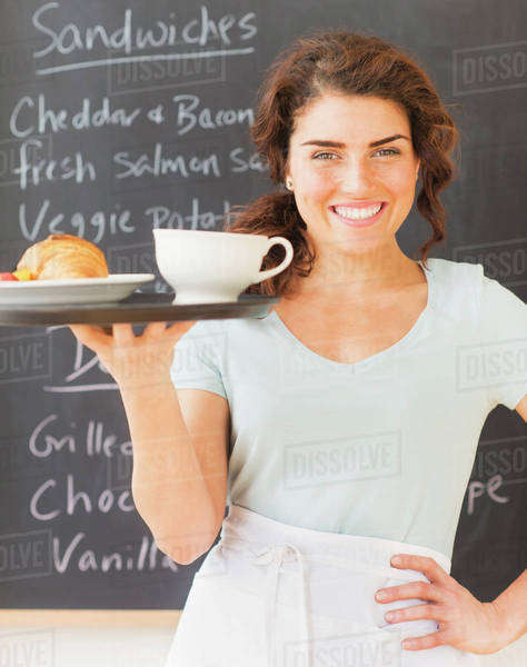 Portrait of smiling waitress with tray against blackboard with menu ...