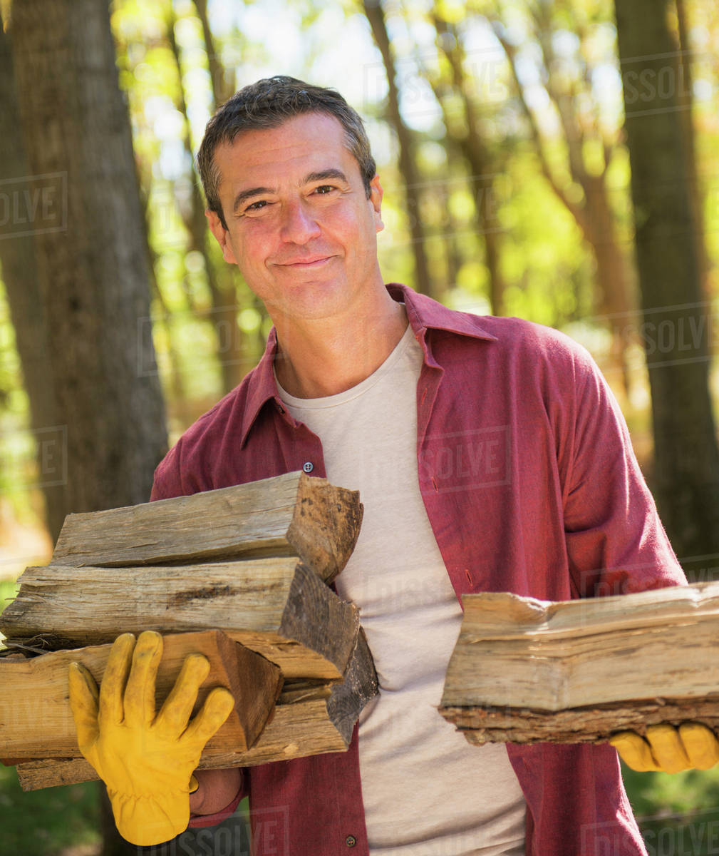 Portrait of Man holding armful of logs - Stock Photo - Dissolve