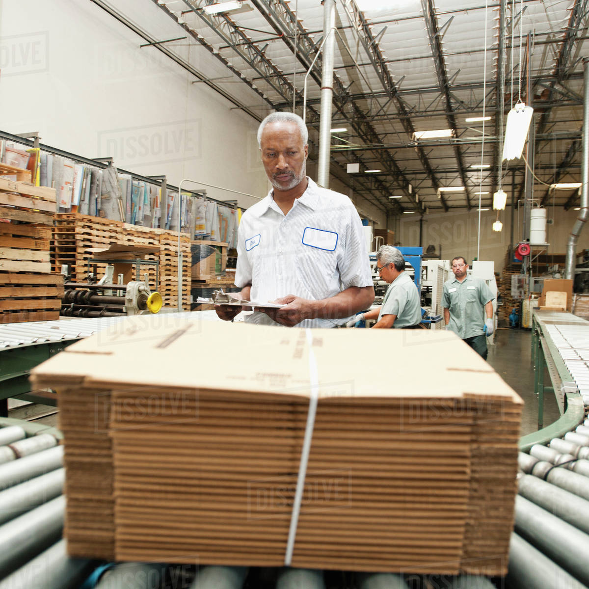 Worker inspecting bundle on conveyor belt - Stock Photo - Dissolve