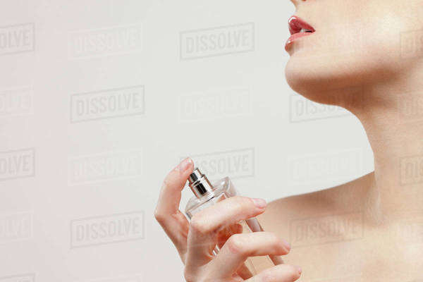 Close up of beautiful young woman spraying perfumes, studio shot ...