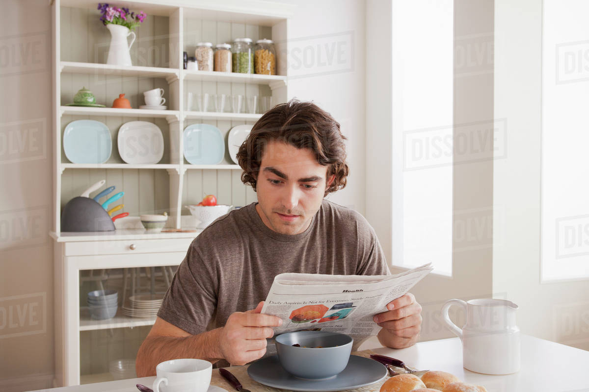 Young man reading newspaper at breakfast - Stock Photo - Dissolve