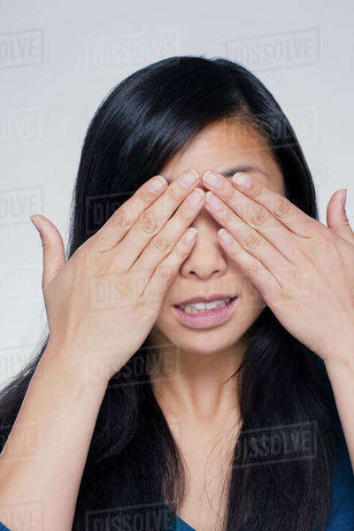 Studio portrait of young woman covering eyes - Stock Photo - Dissolve