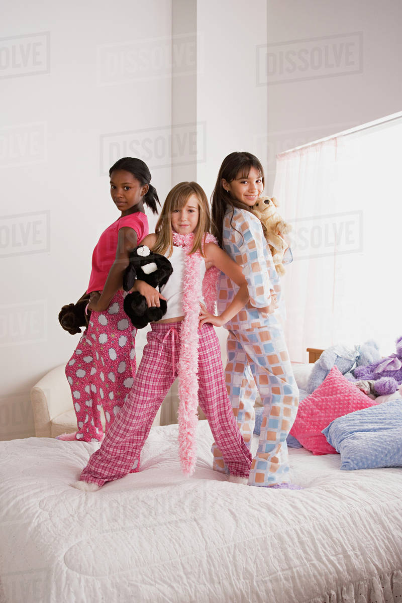 Portrait of three girls (10-11) standing on bed at slumber party ...