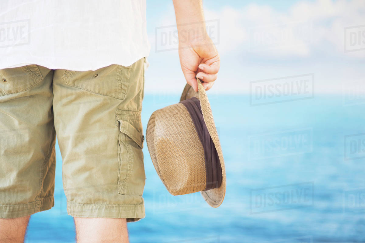 Studio Shot Rear view of man holding straw hat - Stock Photo - Dissolve