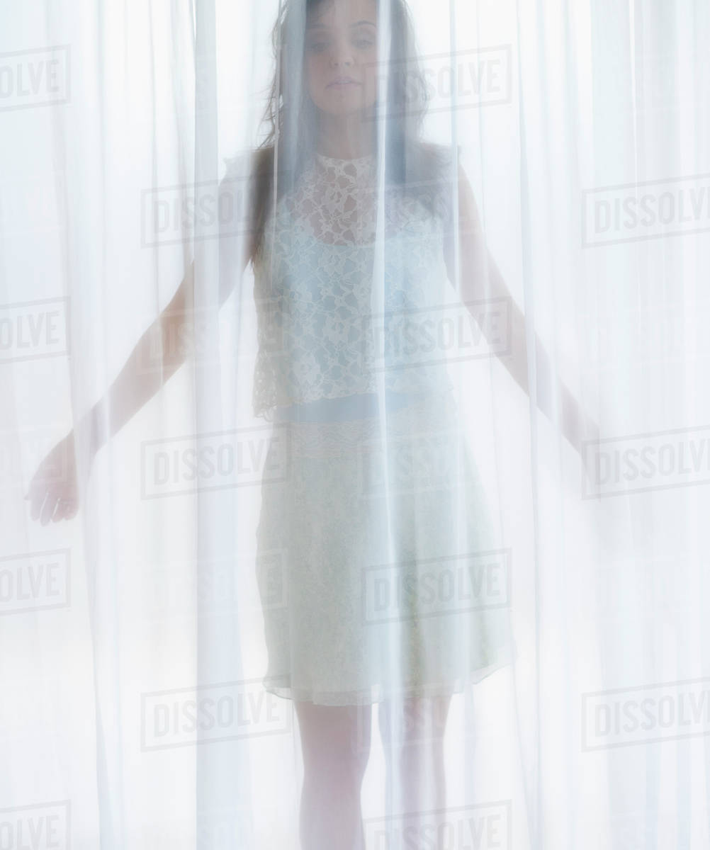 Portrait of young woman behind curtain - Stock Photo - Dissolve