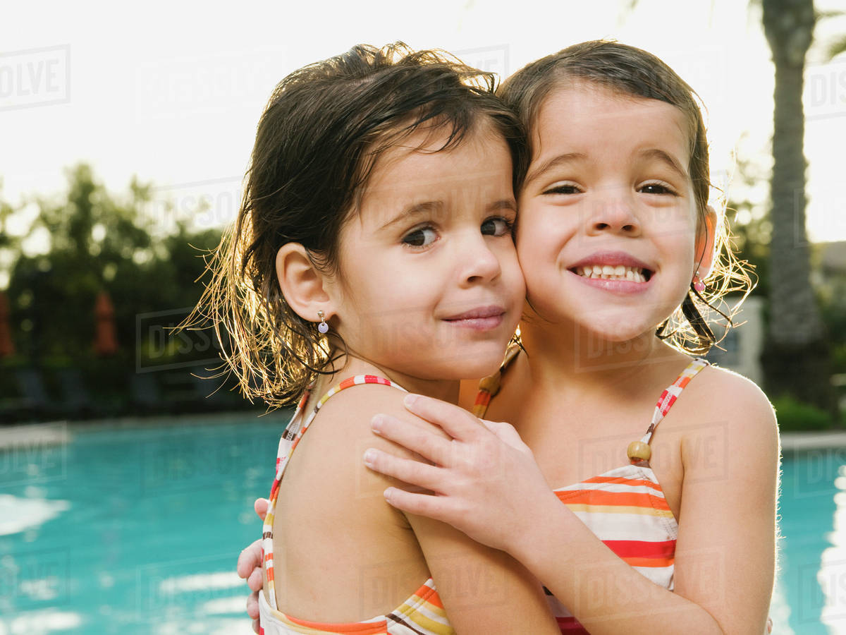 Sister embracing beside pool - Stock Photo - Dissolve