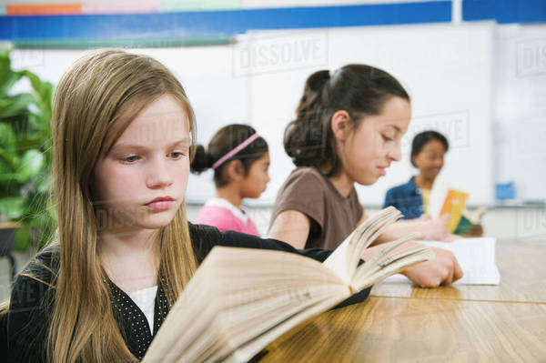 Elementary school students reading books at desk - Stock Photo - Dissolve