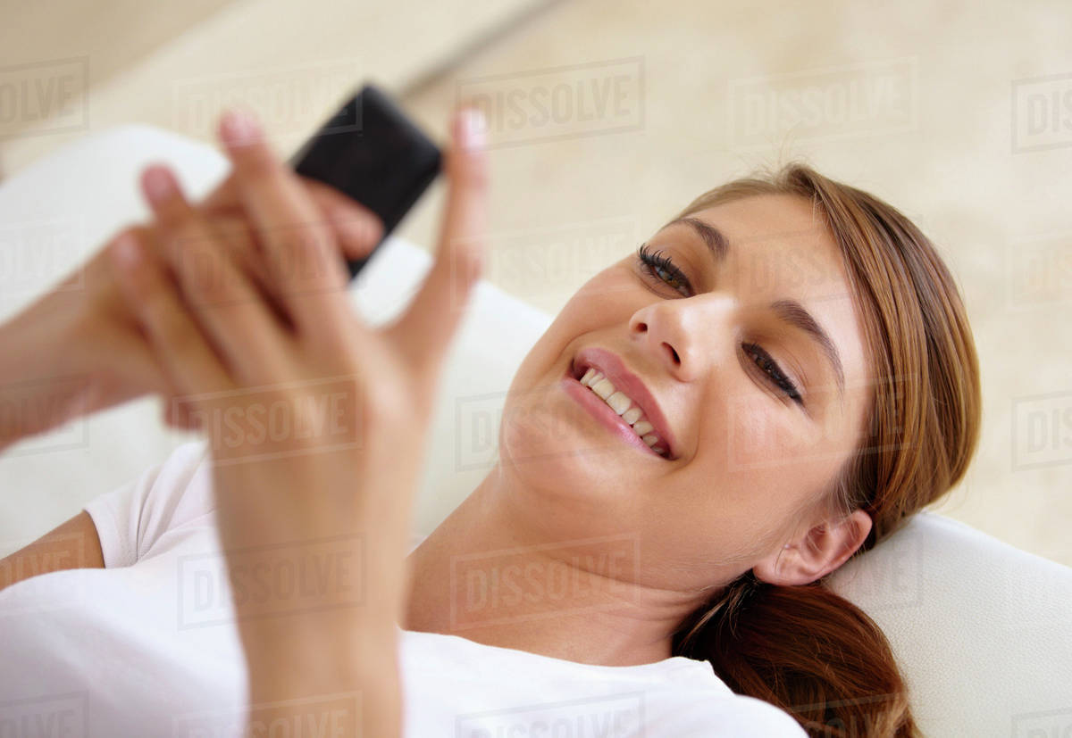Young woman lying on bed and using cell phone - Royalty-free Stock ...
