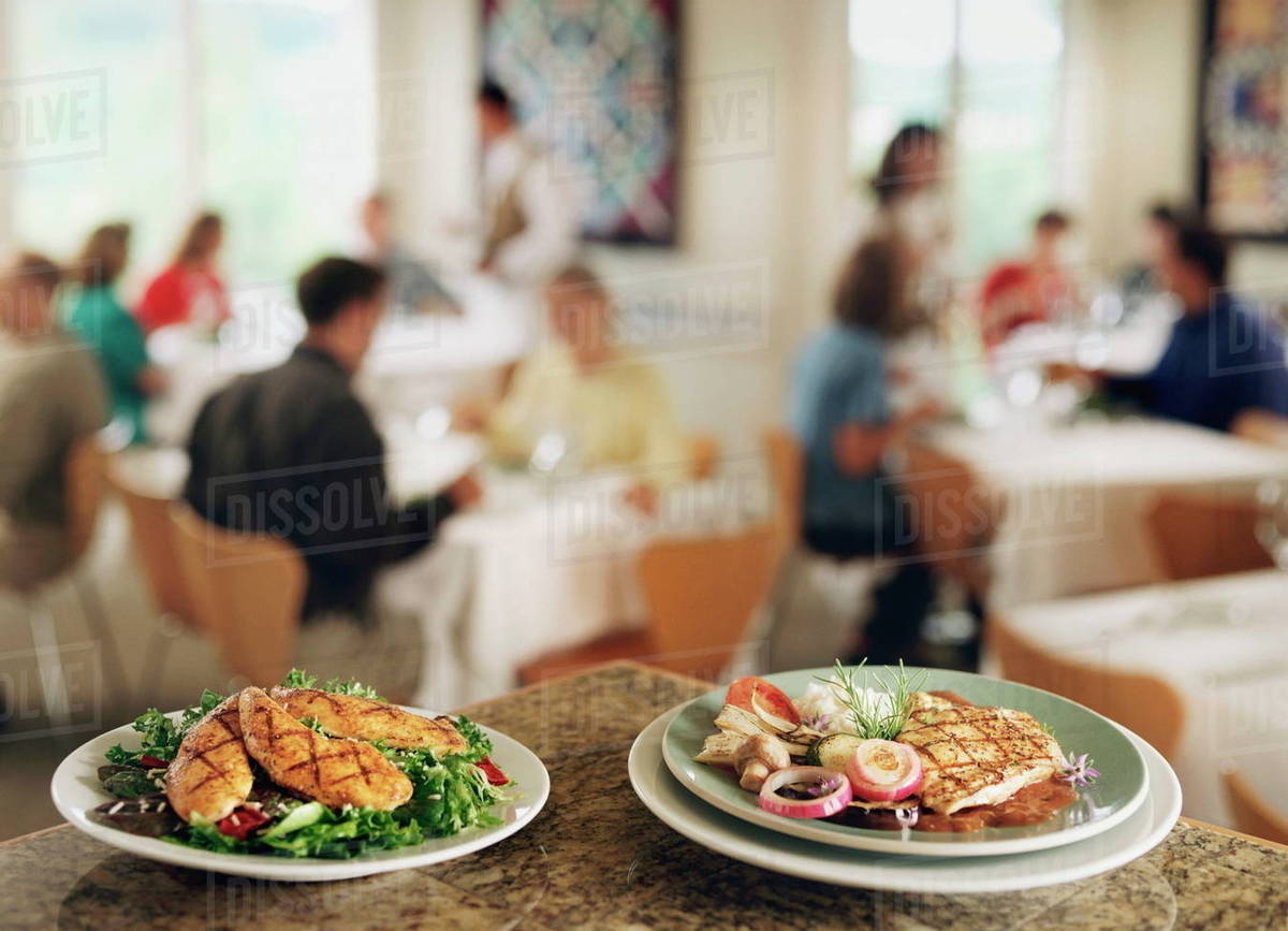Plates with food on bar counter in restaurant, people in background ...