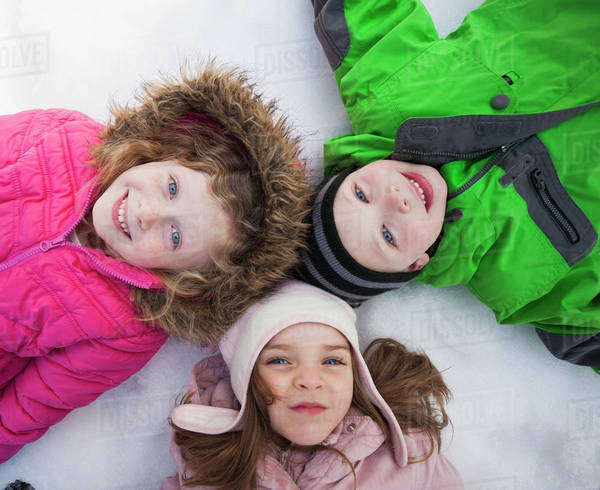 Directly above portrait of three children (2-3, 4-5) lying on snow ...