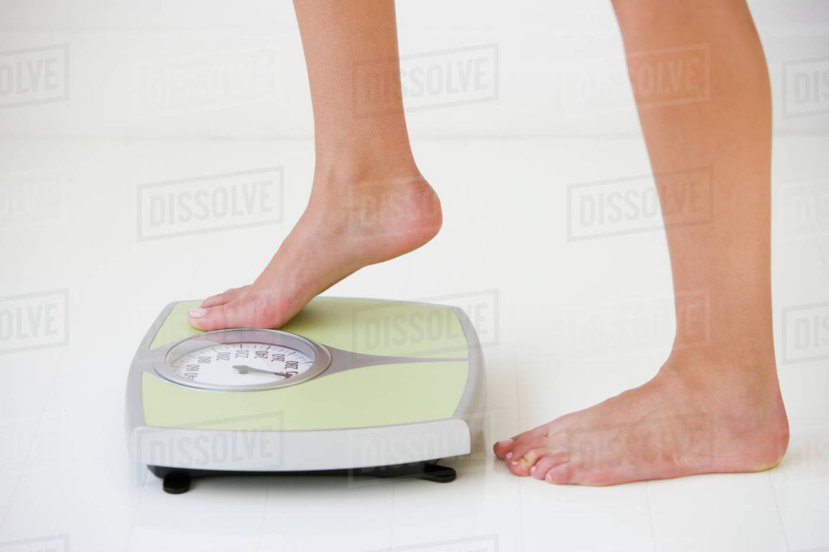 Woman stepping on scale - Stock Photo - Dissolve
