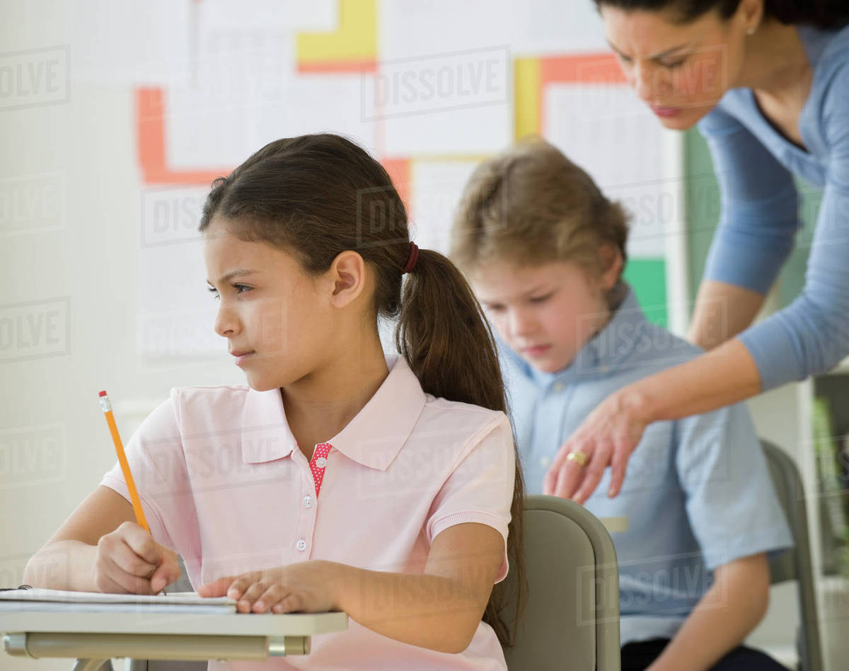 Hispanic girl writing at school desk - Royalty-free Stock Photo | Dissolve
