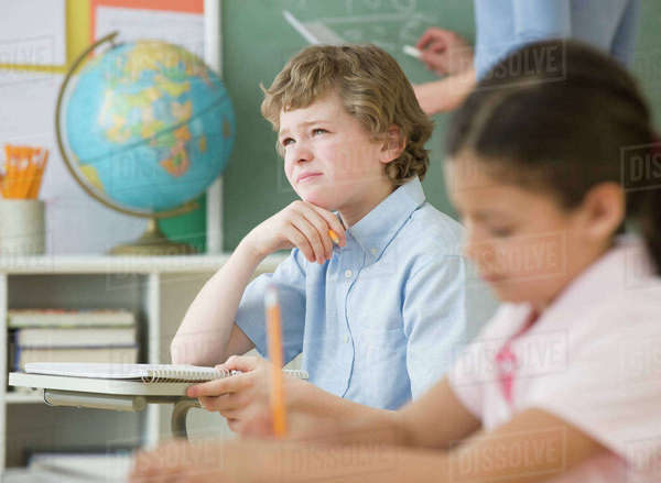 Boy thinking at school desk - Royalty-free Stock Photo | Dissolve